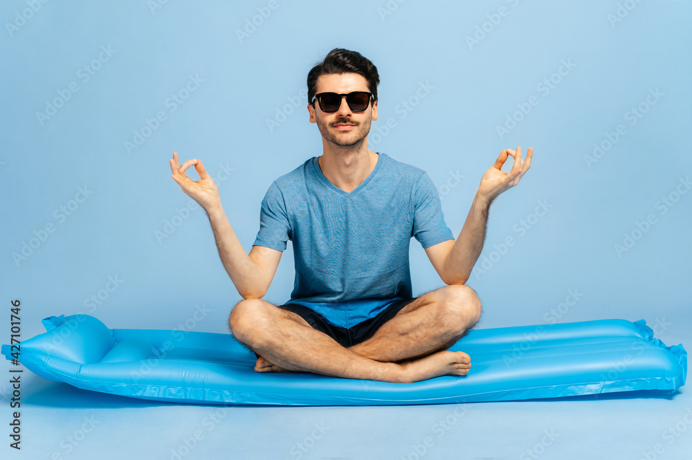 Charismatic caucasian satisfied guy with sunglasses, barefoot, sits on ...