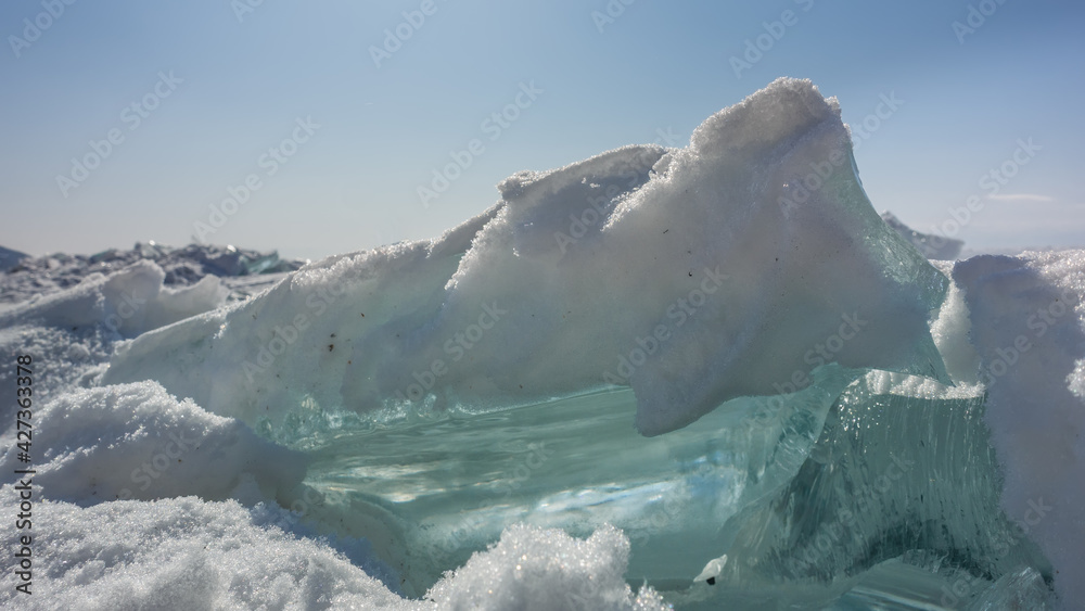 Large transparent turquoise ice hummock on a frozen lake. The ice floe ...