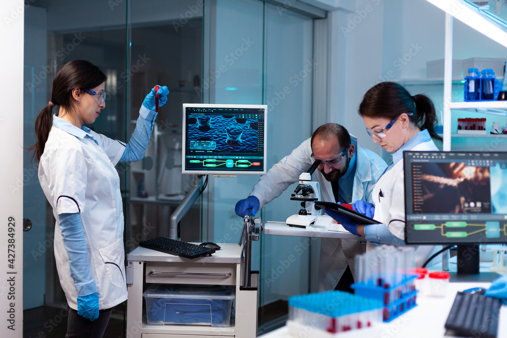 Scientist analyzing blood sample in vacutainer with researching team ...