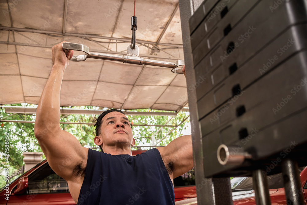 A fit asian guy working out as his garage, doing lat pulldowns using a ...
