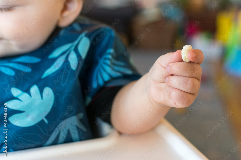Baby holding a cereal puff in their hand using pincer grasp ...