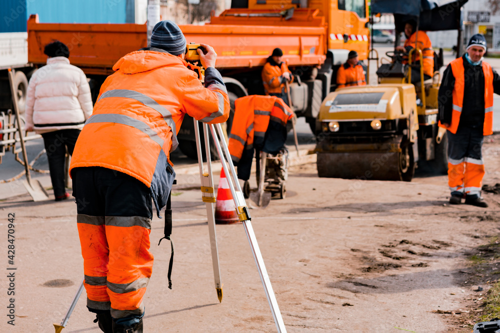 Municipal worker in orange jacket measuring via optical level on ...