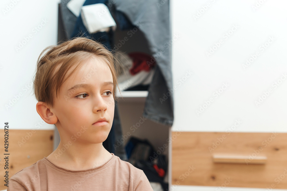 Boy standing near messy clothes on shelf. Preteen boy with dirty ...