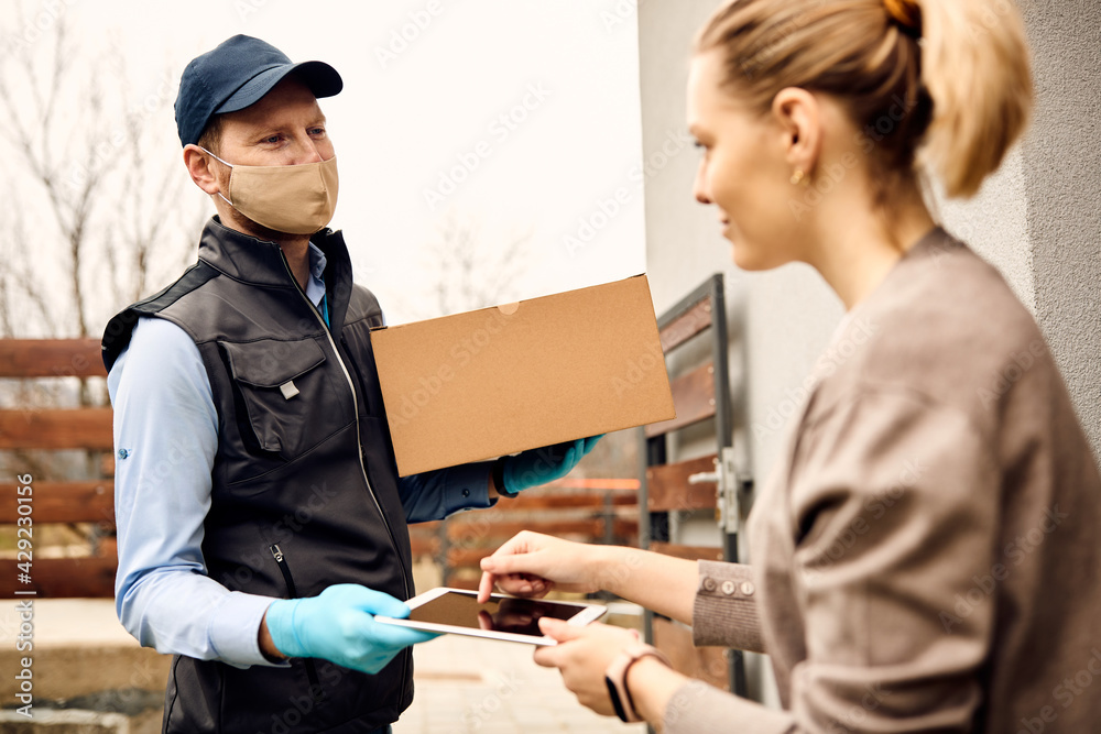Female customer signing on digital device to courier who is wearing ...