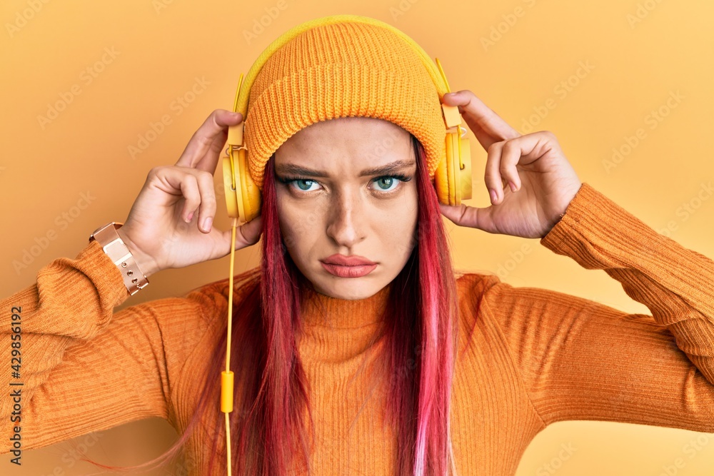 Young caucasian woman listening to music using headphones depressed and ...
