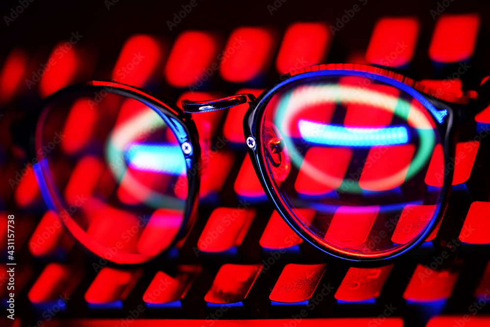 Glasses in black frame lie on a keyboard glowing in the dark ...