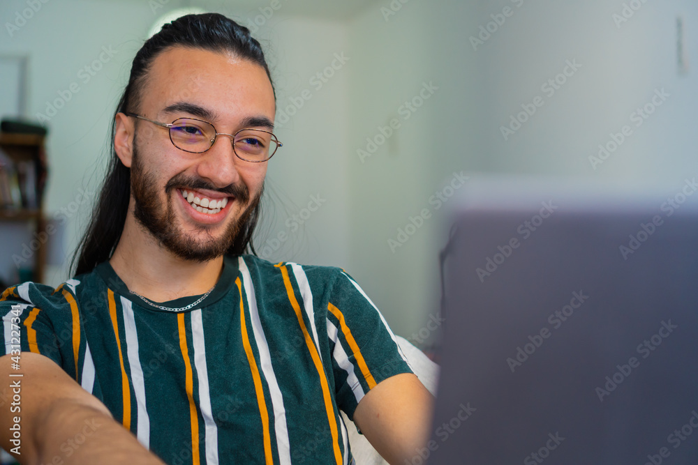 young latin long haired man laughing happily, while using the computer ...