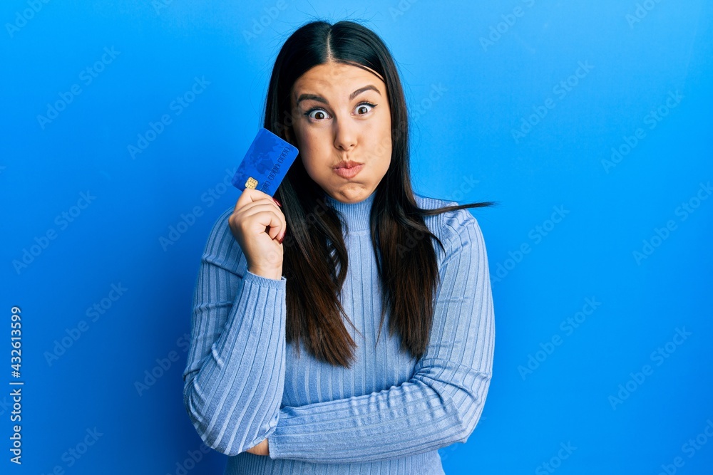 Beautiful brunette woman holding credit card puffing cheeks with funny ...