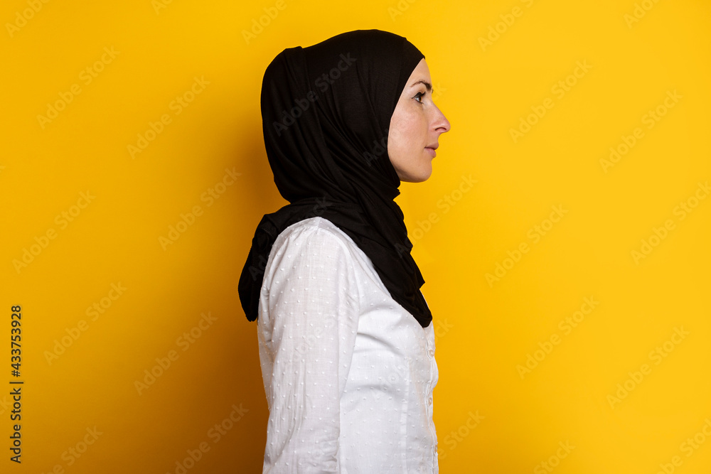 Young Muslim woman in hijab looks to the side on a yellow background ...