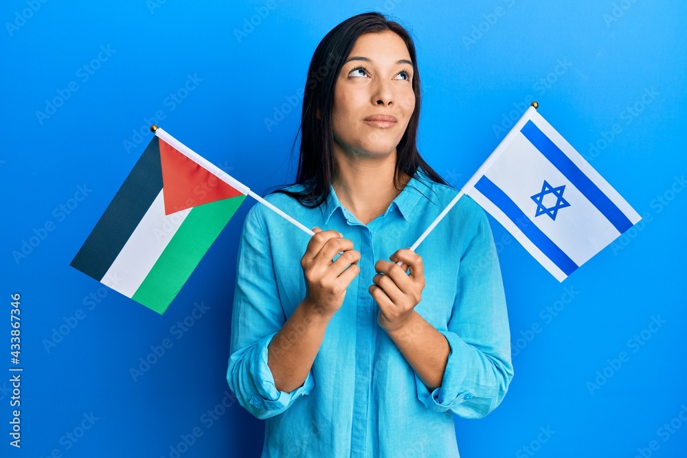 Young latin woman holding palestine and israel flags smiling looking to ...