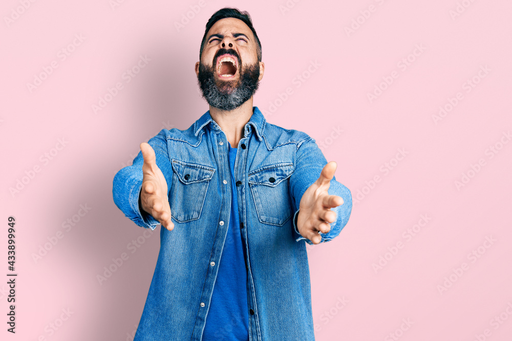Hispanic man with beard with open arms doing hug gesture angry and mad ...