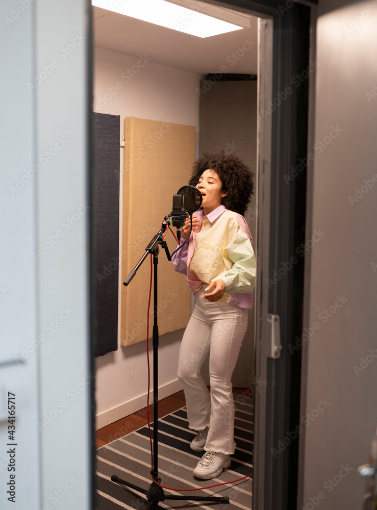 Black female singer performing song against microphone with pop filter ...