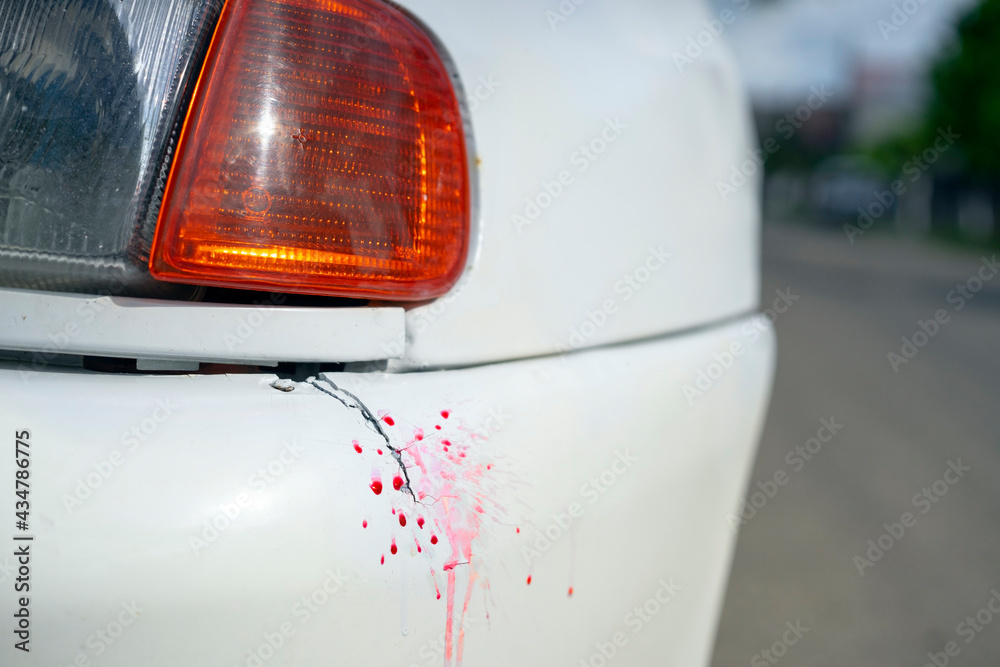 A crack and drops of blood on the front bumper of a white old car ...