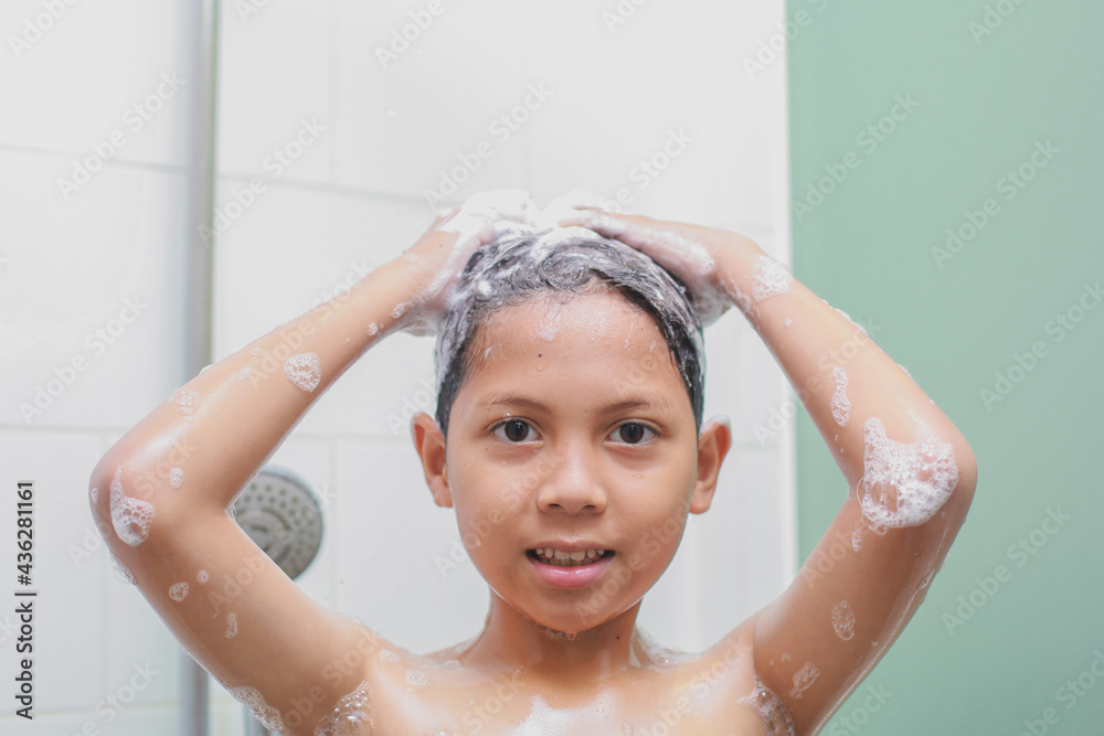 Smiling boy rubbing hair using shampoo during shower in the bathroom ...