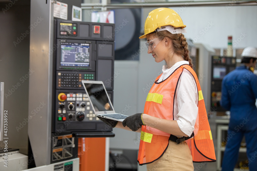Factory worker is programming a CNC milling machine with a tablet computer. engineering and ...