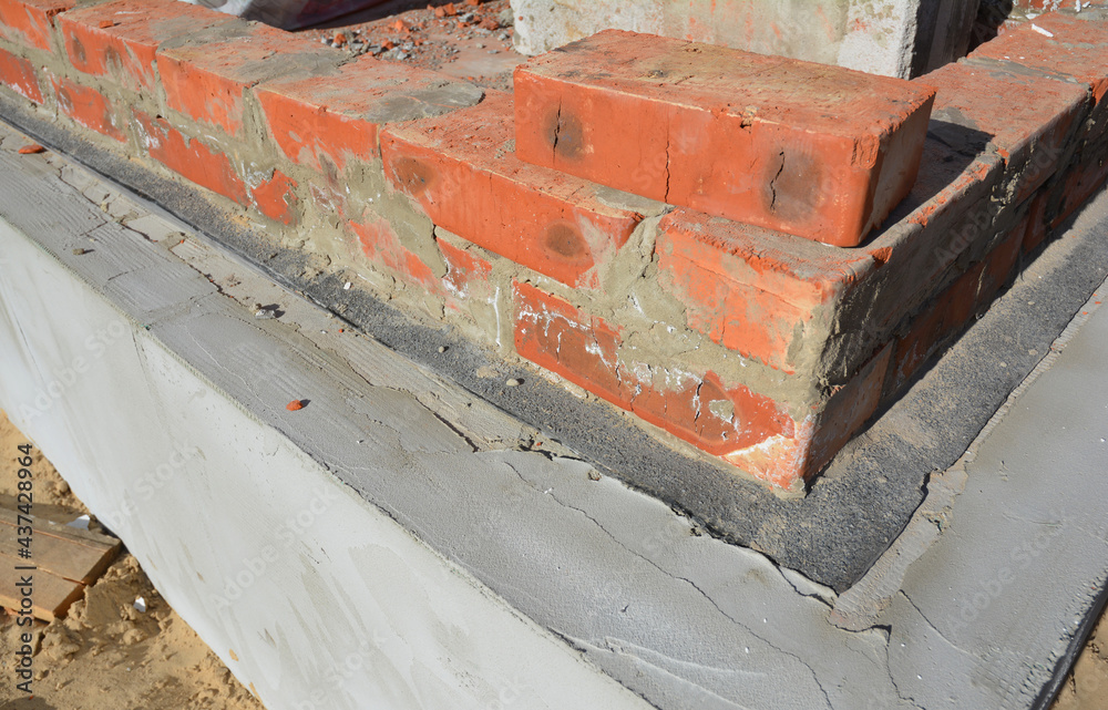 A close-up of bricklaying a house wall corner with the first course of ...