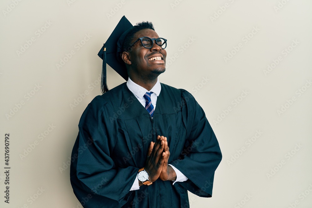 Handsome black man wearing graduation cap and ceremony robe begging and ...