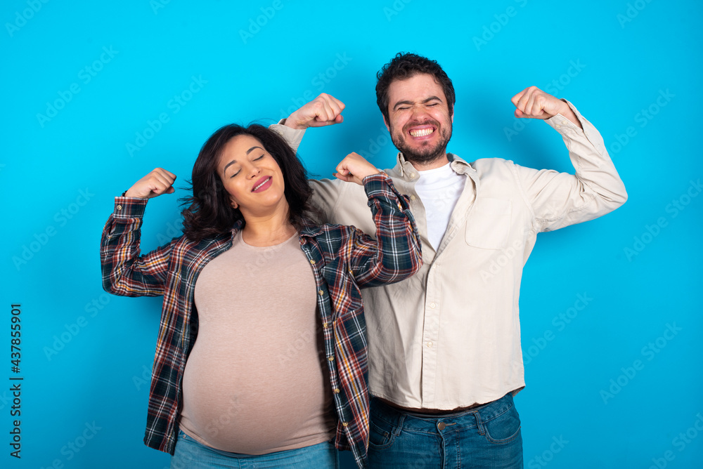 Strong powerful young couple expecting a baby standing against blue ...