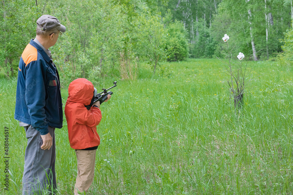 Back view of a boy in a red windbreaker is aiming an air gun with a ...