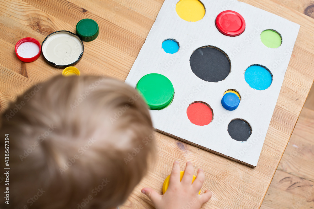 find a match. child inserting different size and color plastic caps in matching holes.ergo ...