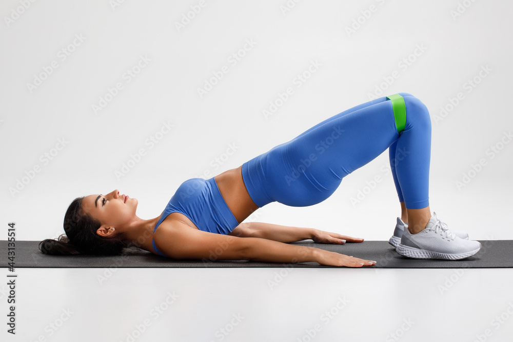 Fitness woman doing glute bridge exercise with resistance band on gray ...