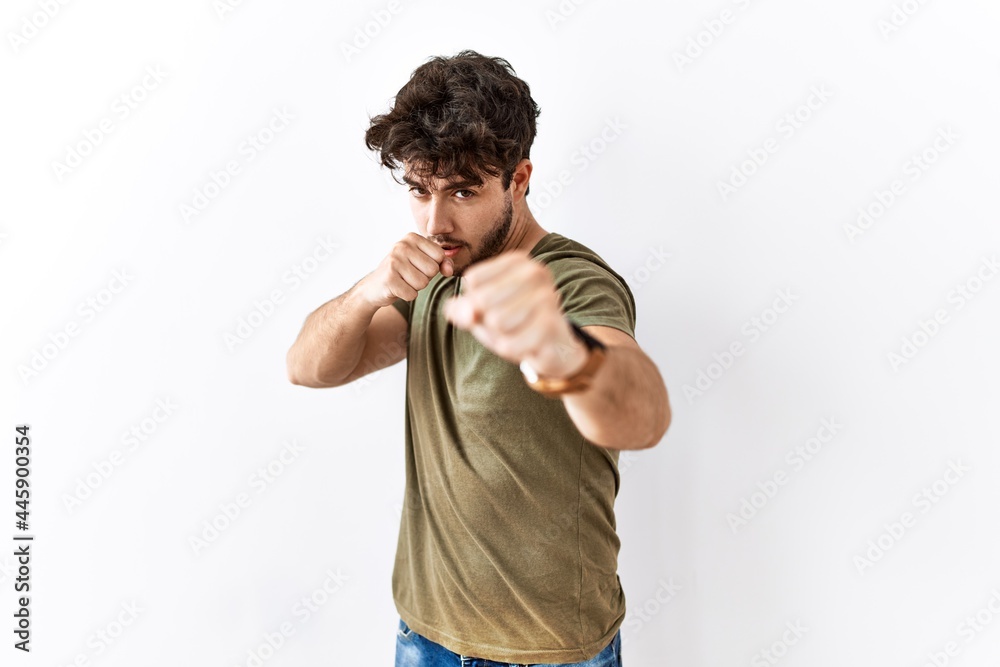 Hispanic man standing over isolated white background punching fist to ...