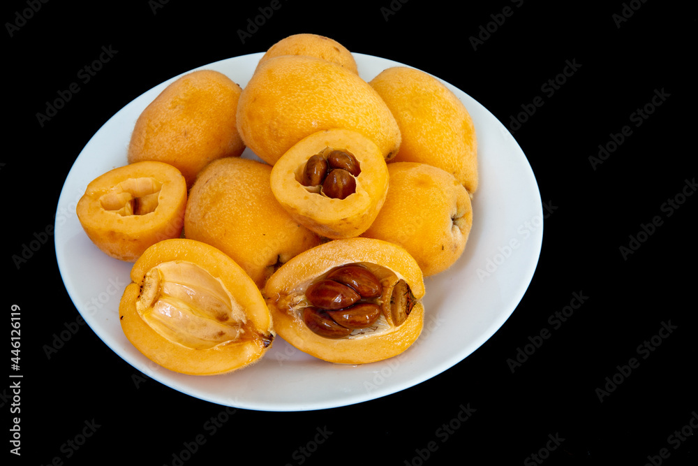 loquats on white plate on black background top view. One cut in half ...