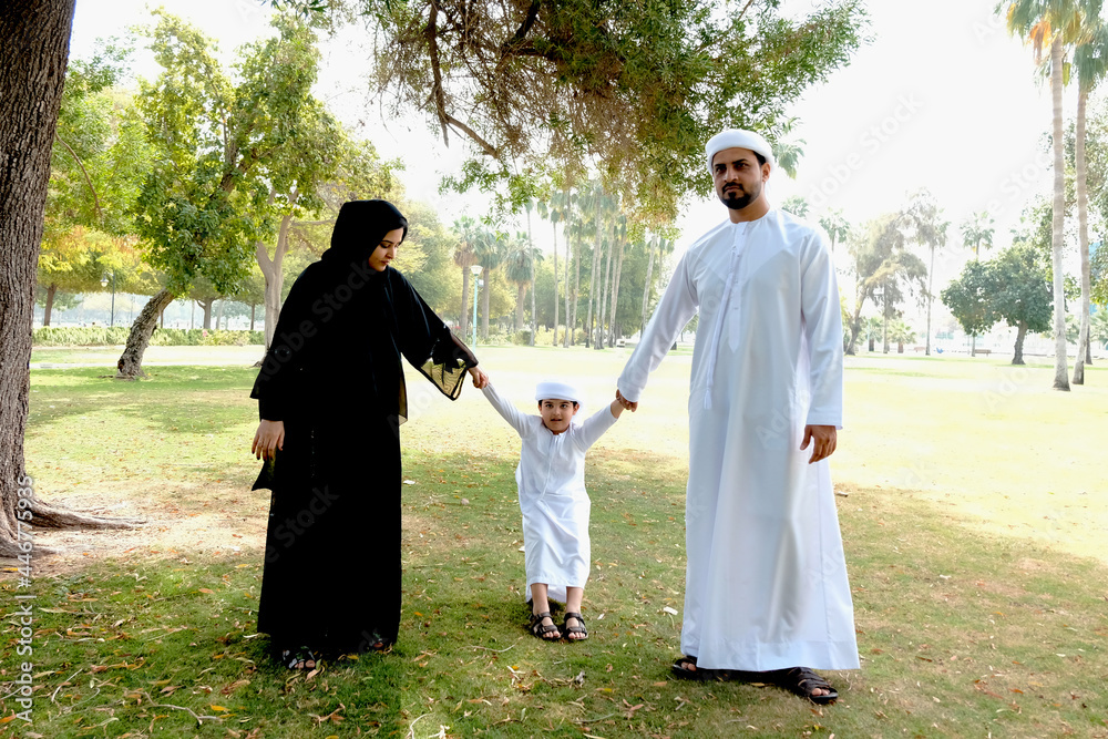 Arab family walking together. Emirati man with his wife and son walks forward wearing ...