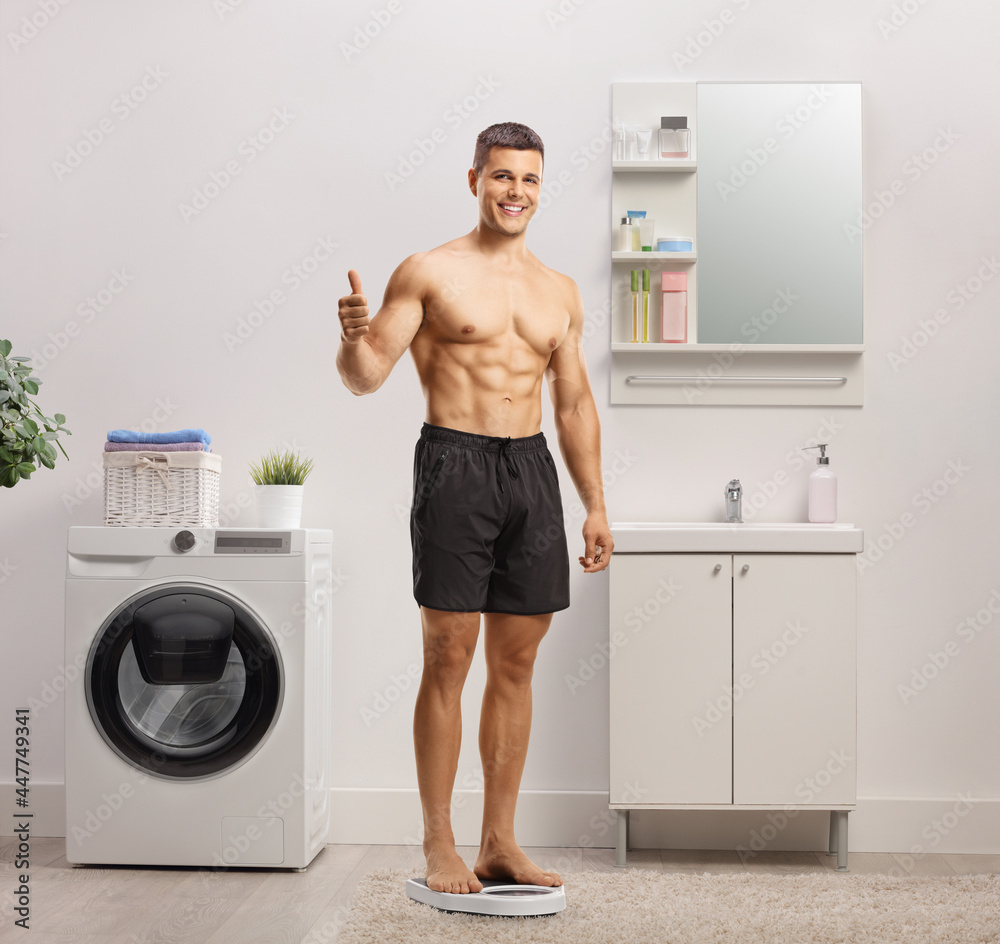 Young smiling shirtless man standing on a weigth scale in a bathroom ...