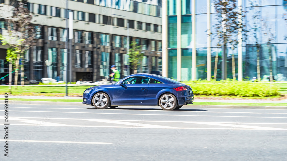 Blue Audi TT Mk2 is driving on high speed in front of modern buildings ...