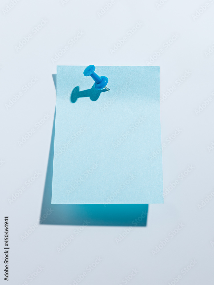 Blank blue sticky note pinned on a bright blue wall background. Office ...