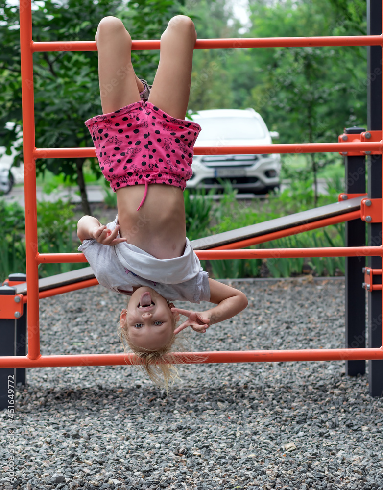 girl 6-7 years old is playing cheerfully on the playground, hanging upside down Stock Photo ...