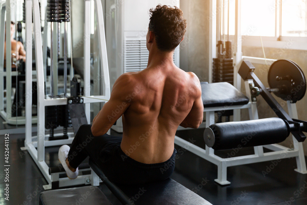 Muscular man doing exercise and pulling weights in seated cable row ...