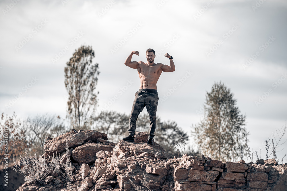 Bodybuilder posing outdoor. Man standing at the rock with tensed ...