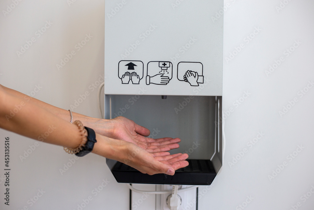 Woman's hands near non-contact antiseptic dispenser. Disinfection of ...