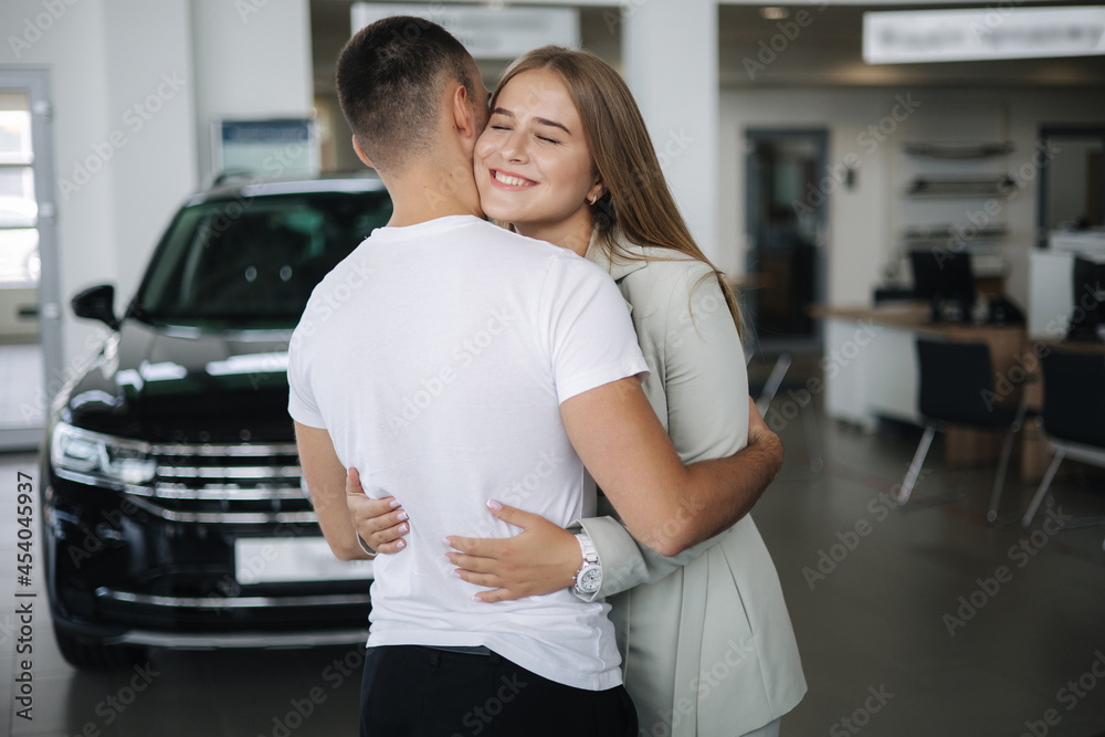 Happy woman hug his husband afrer buying car in car showroom. Man and ...
