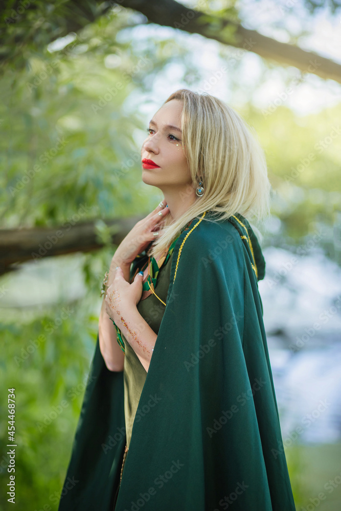 A blonde woman in a green druid cloak and in a fantasy dress with ...