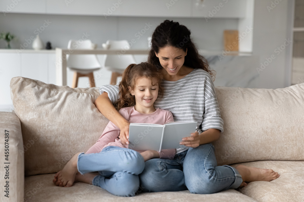 Loving young woman cuddling small adorable kid daughter, reading fairy ...