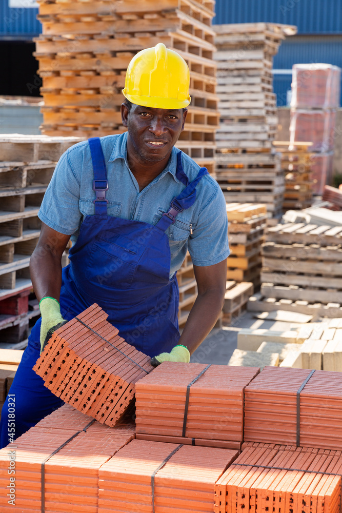African-american male worker carrying clay bricks in outdoor ...