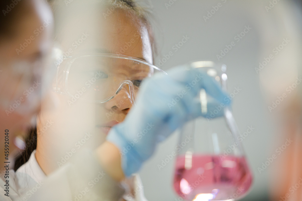 Girl student examining pink liquid, conducting scientific experiment in ...