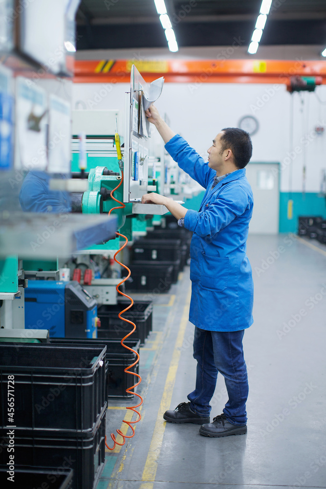 Worker at small parts manufacturing factory in China, reaching up to ...