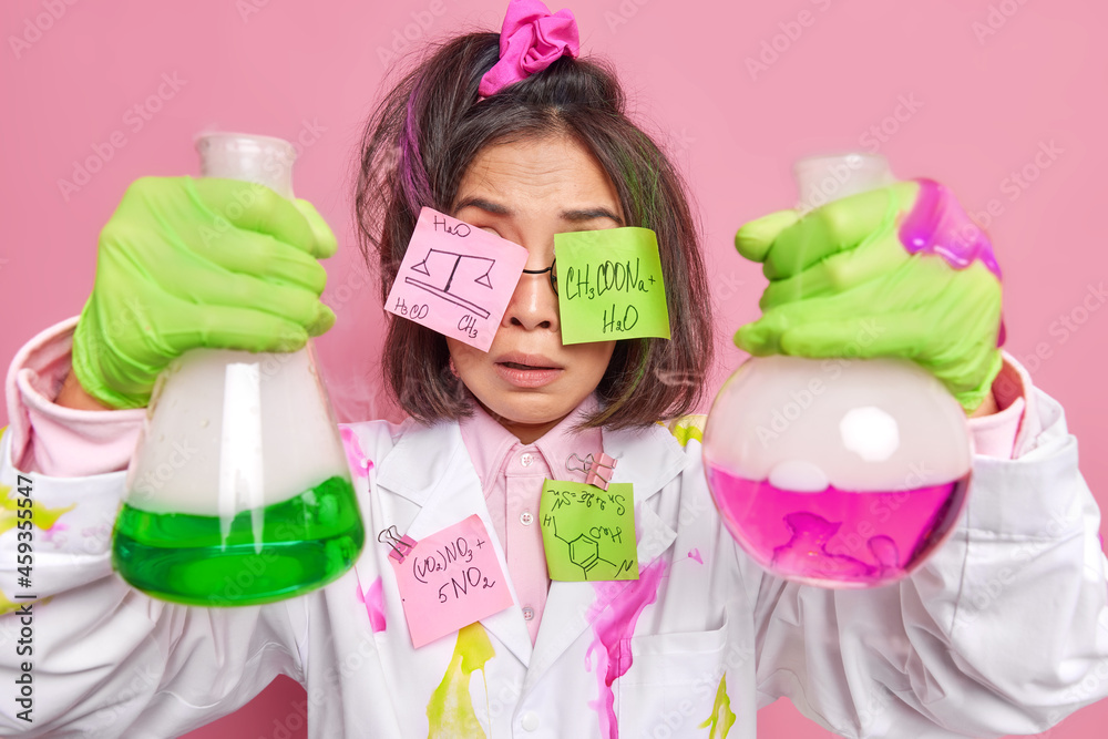 Female chemist holds glass flasks with colorful liquid wears medical ...