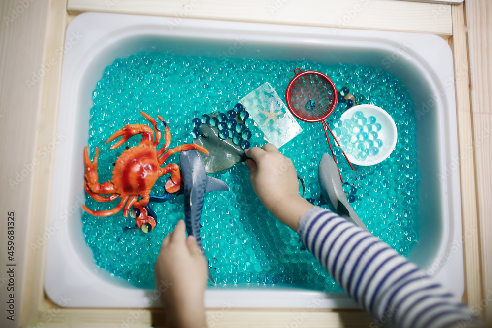Hydrogel sensory box, baby hands play with blue hydrogel and marine ...