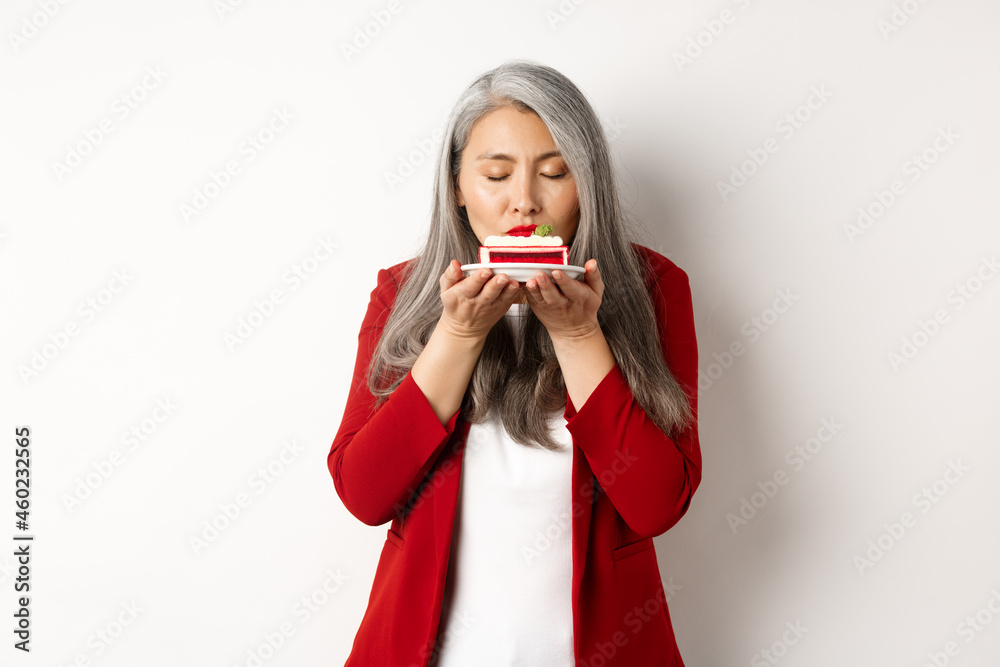Image of funny asian senior lady sniffing delicious cake, smell dessert ...