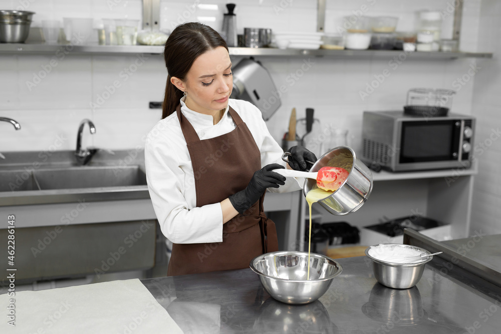 Female pastry chef pours melted white chocolate from a saucepan into a ...