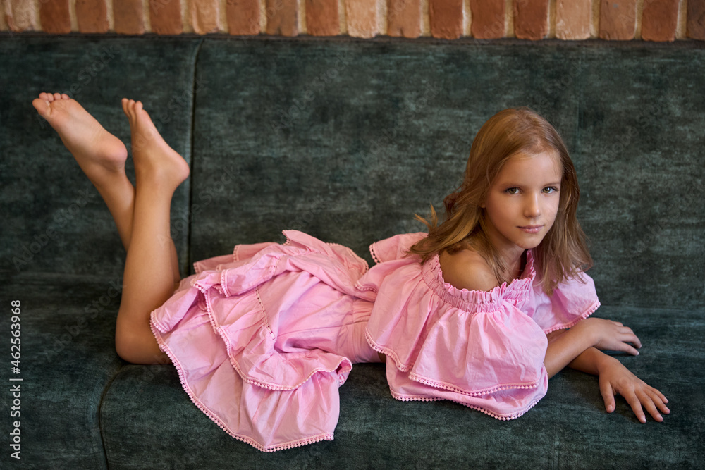 Foto de Stock Teen girl in a pink stylish dress and bare feet lies on the sofa | Adobe Stock