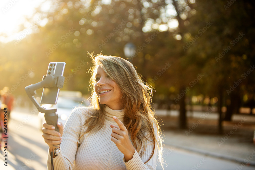 blonde girl smiling and filming herself outdoors with cell phone and ...