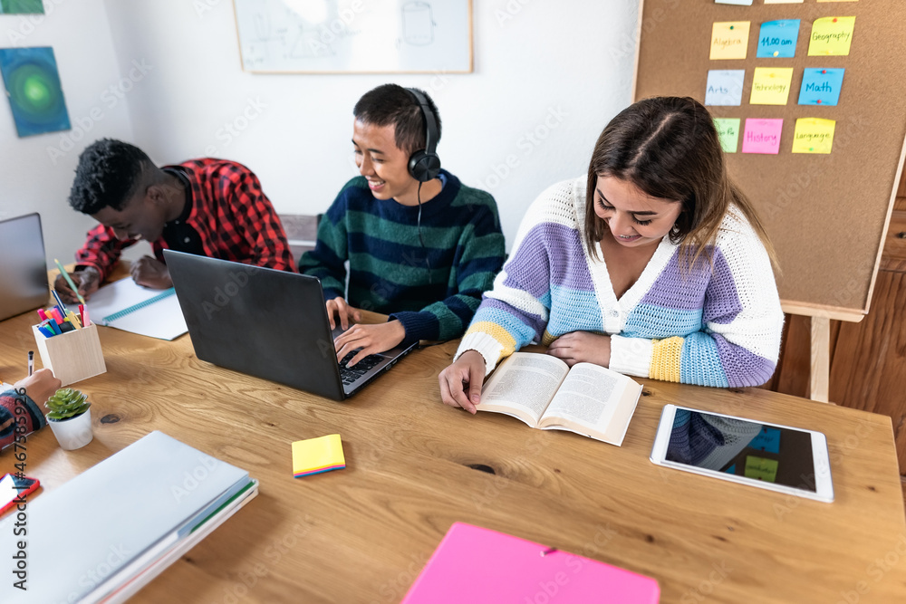 Young multiracial students reading books and using laptop in classroom ...