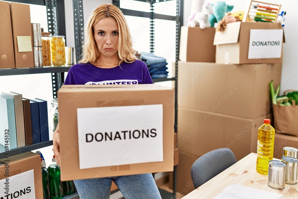 Beautiful blonde woman volunteer holding donations box depressed and ...