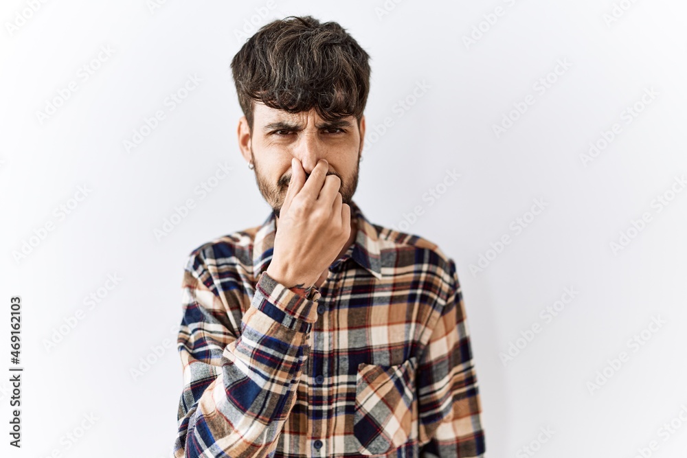 Hispanic man with beard standing over isolated background smelling ...